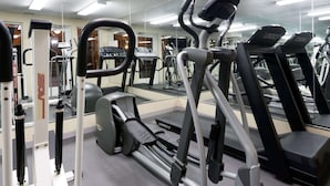 Uma academia com equipamentos de cardio, espelhos e esteira.