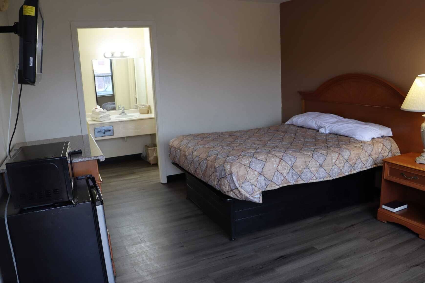 Quarto de hotel com cama, escrivaninha, abajur e espelho.