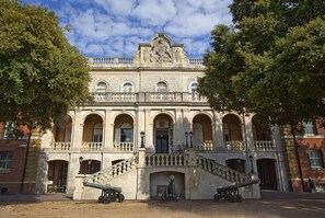 Um edifício histórico com entrada central, janelas em arco e escadaria que leva à entrada.