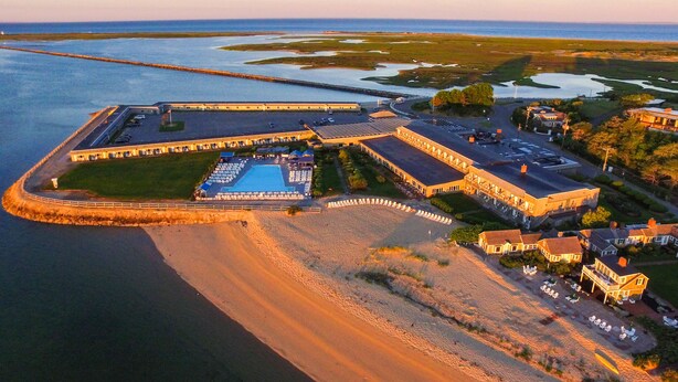 Vista aérea de um resort à beira-mar, com uma piscina grande, vários edifícios e uma área de praia.