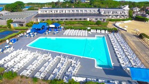 Vista aérea de um resort com uma piscina grande, cercada por espreguiçadeiras e uma área coberta com mesas e cadeiras.