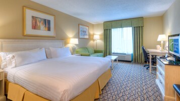 Quarto de hotel com uma cama grande, uma escrivaninha, uma cadeira, uma televisão e uma janela com cortinas.