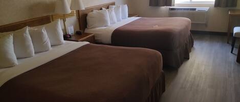 Quarto de hotel com duas camas, uma escrivaninha, uma cadeira e uma janela com cortinas.