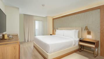 Quarto de hotel com uma cama grande, mesa de cabeceira, luminária e televisão sobre um suporte.