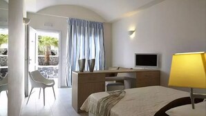 Quarto com cama, escrivaninha, cadeira, televisão e janela com cortinas.