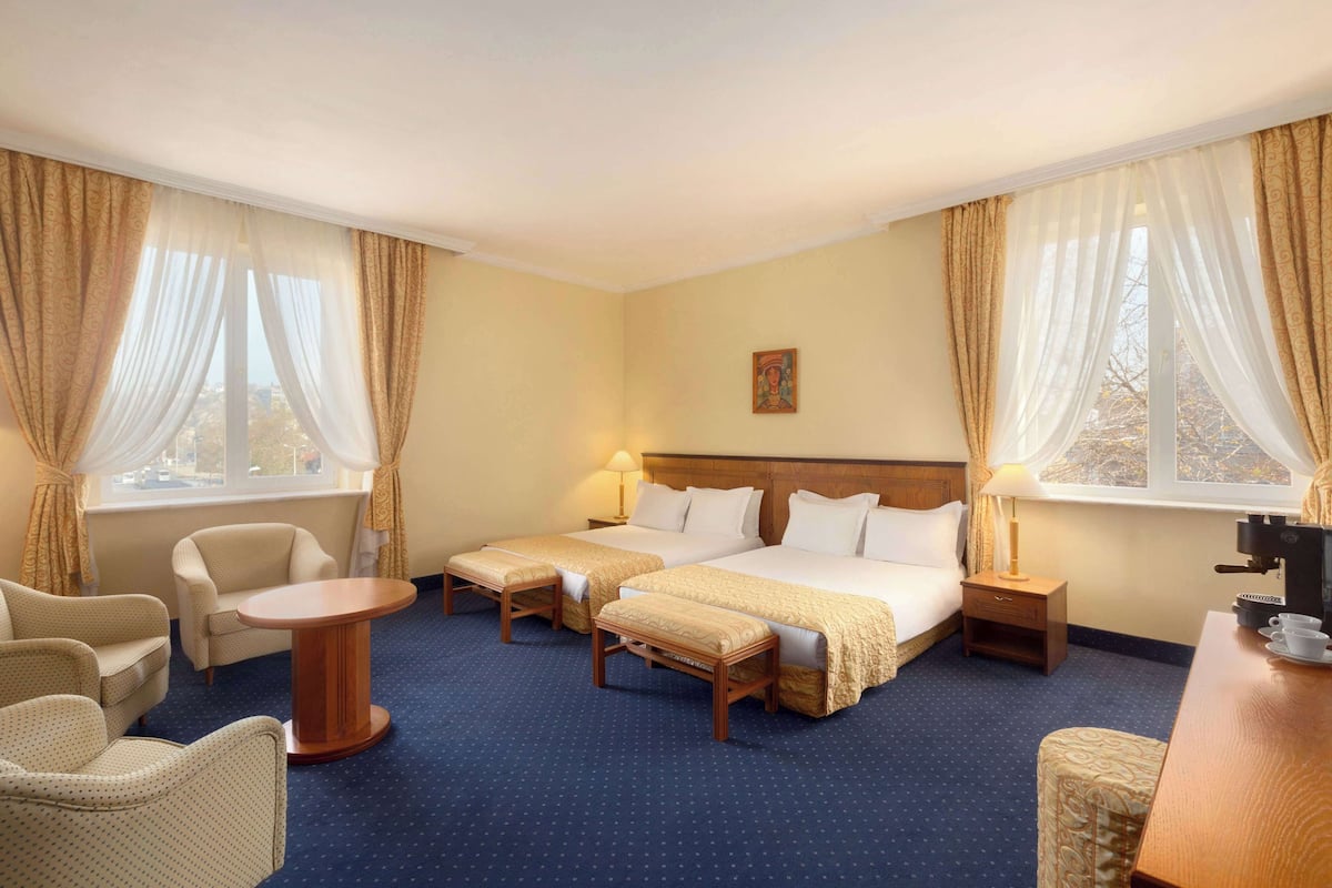 Quarto de hotel com duas camas, uma mesa pequena, uma cadeira e uma escrivaninha.