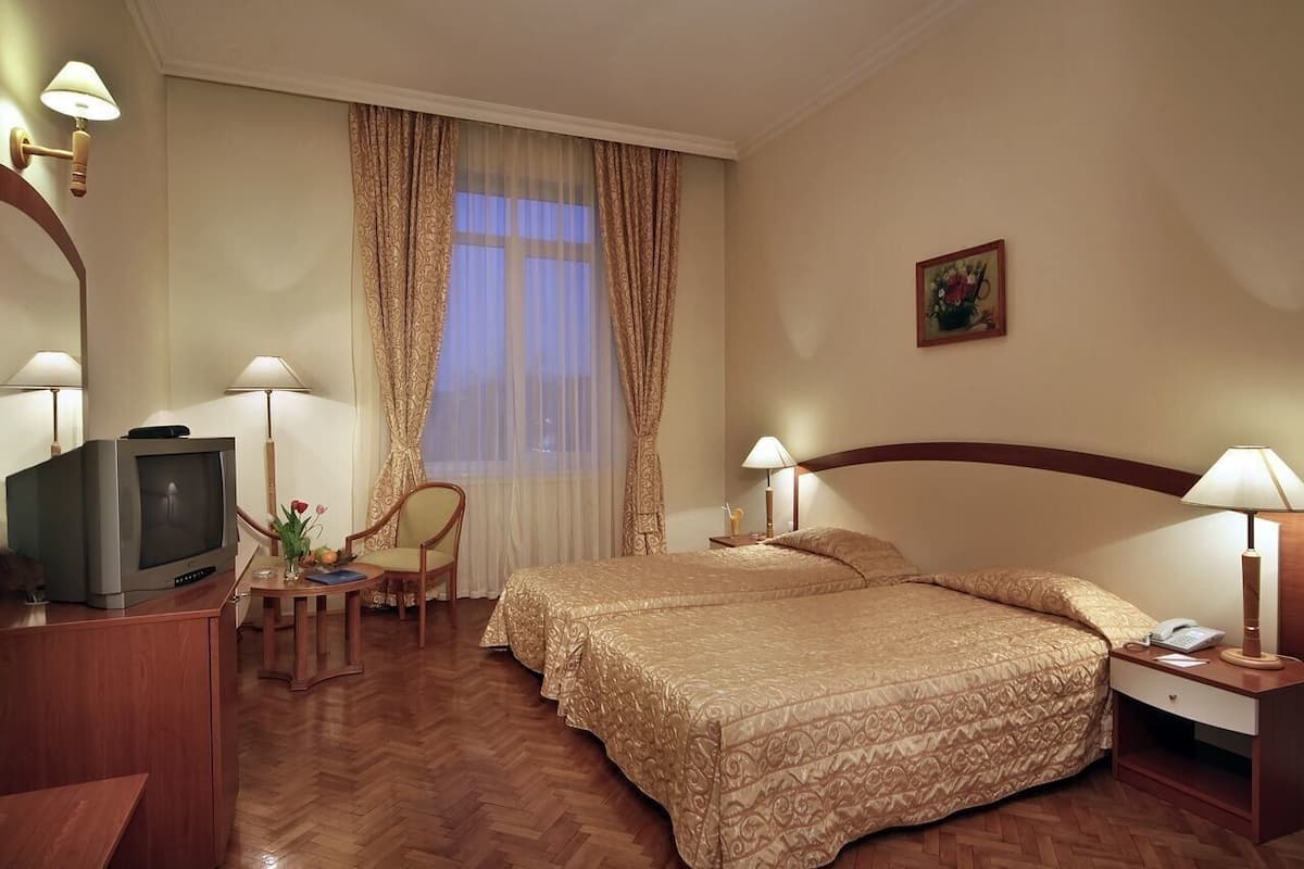 Quarto de hotel com duas camas, televisão, escrivaninha com candeeiro e uma cadeira.