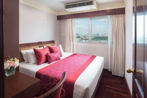 Quarto de hotel com uma cama grande, uma mesa de cabeceira com um vaso de flores e vista para a cidade pela janela.