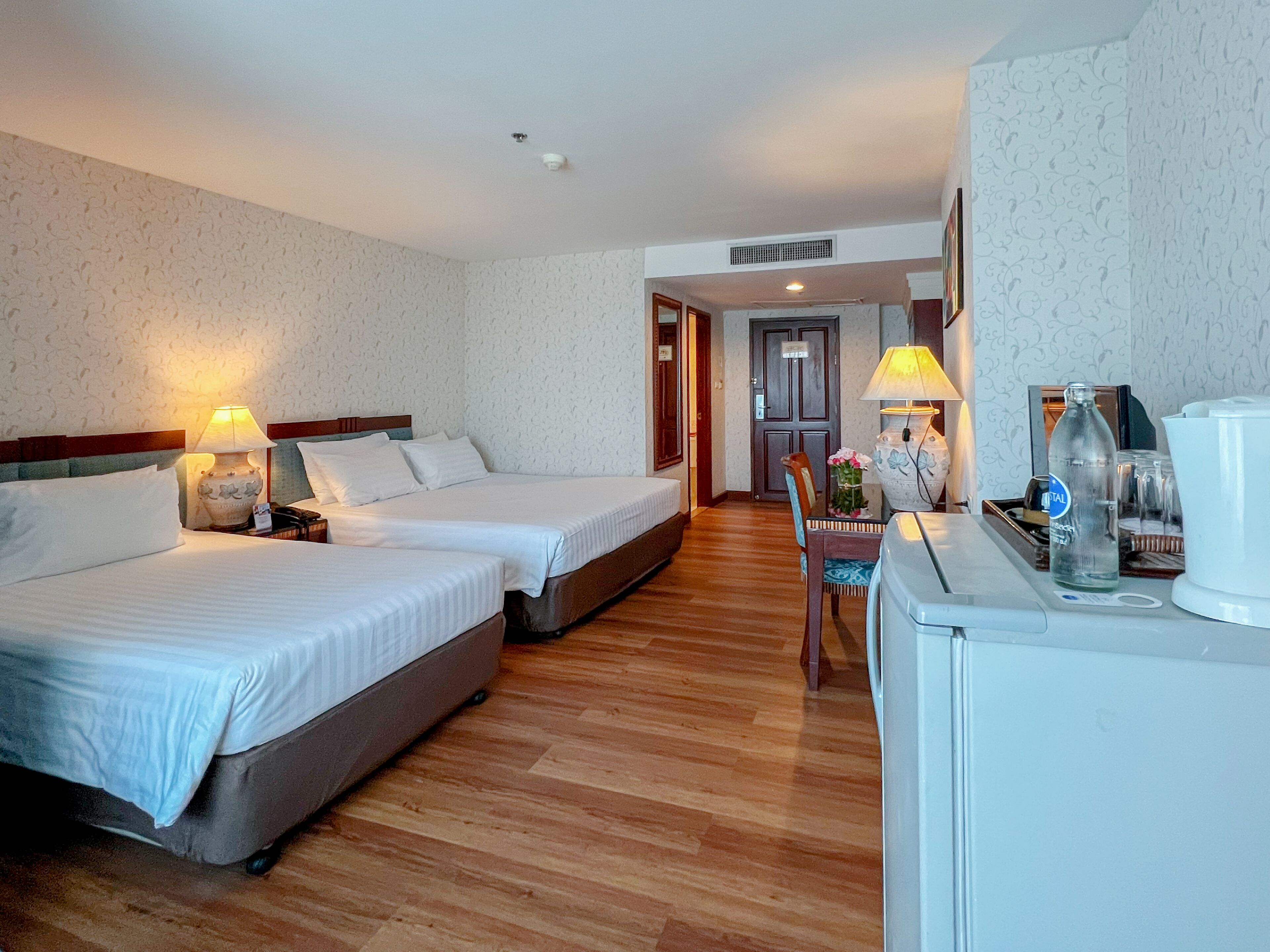 Quarto de hotel com duas camas, uma escrivaninha com abajur, uma cafeteira e um vaso com flores.