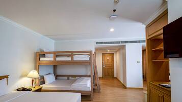 Quarto de hotel com beliches, uma escrivaninha com luminária, um guarda-roupa e uma televisão.