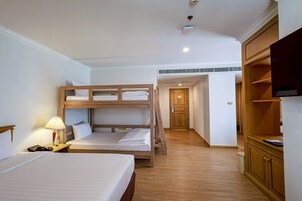 Quarto de hotel com beliches, uma escrivaninha com luminária, um guarda-roupa e uma televisão.