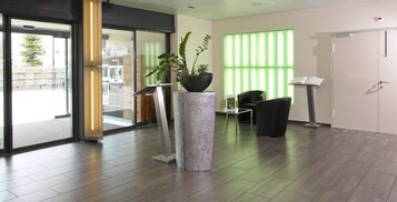 Um lobby moderno com balcão de recepção, planta em vaso, área de estar e porta de vidro que dá para o exterior.