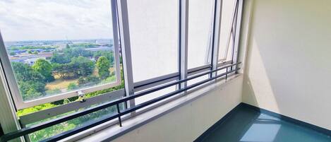 Quarto com amplas janelas que oferecem vista para uma paisagem verde e edifícios.