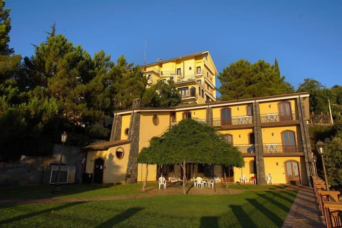 Um edifício amarelo de vários andares com um pátio central, rodeado por árvores e com área de estar ao ar livre.