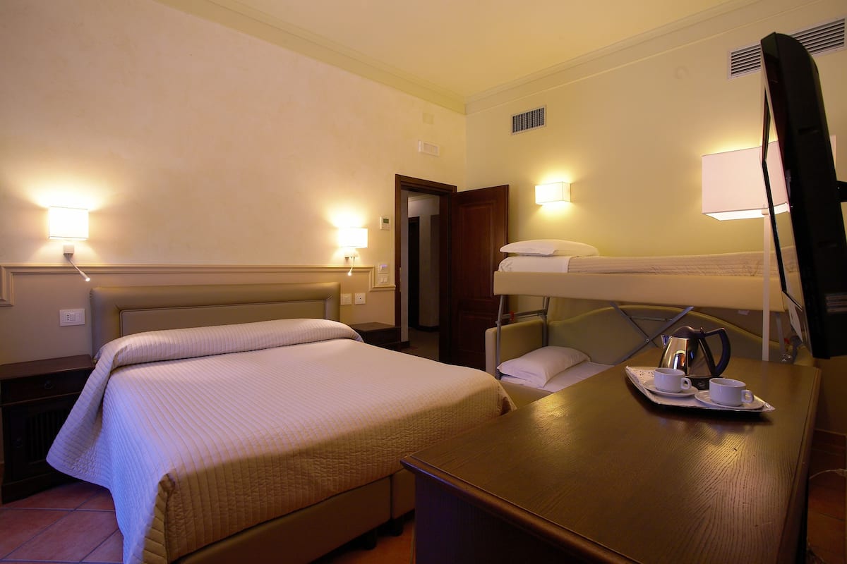 Quarto de hotel com cama, escrivaninha e bandeja com xícaras de café, além de uma televisão.