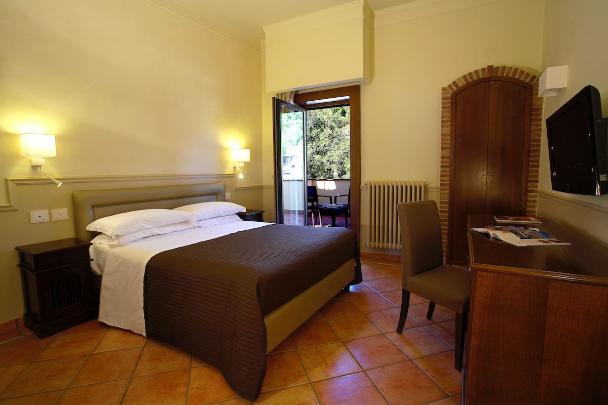 Quarto de hotel com cama, mesas de cabeceira, escrivaninha, cadeira e televisão.