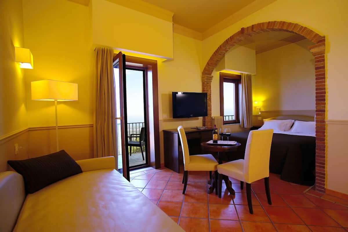 Quarto de hotel com cama, escrivaninha, televisão e varanda.