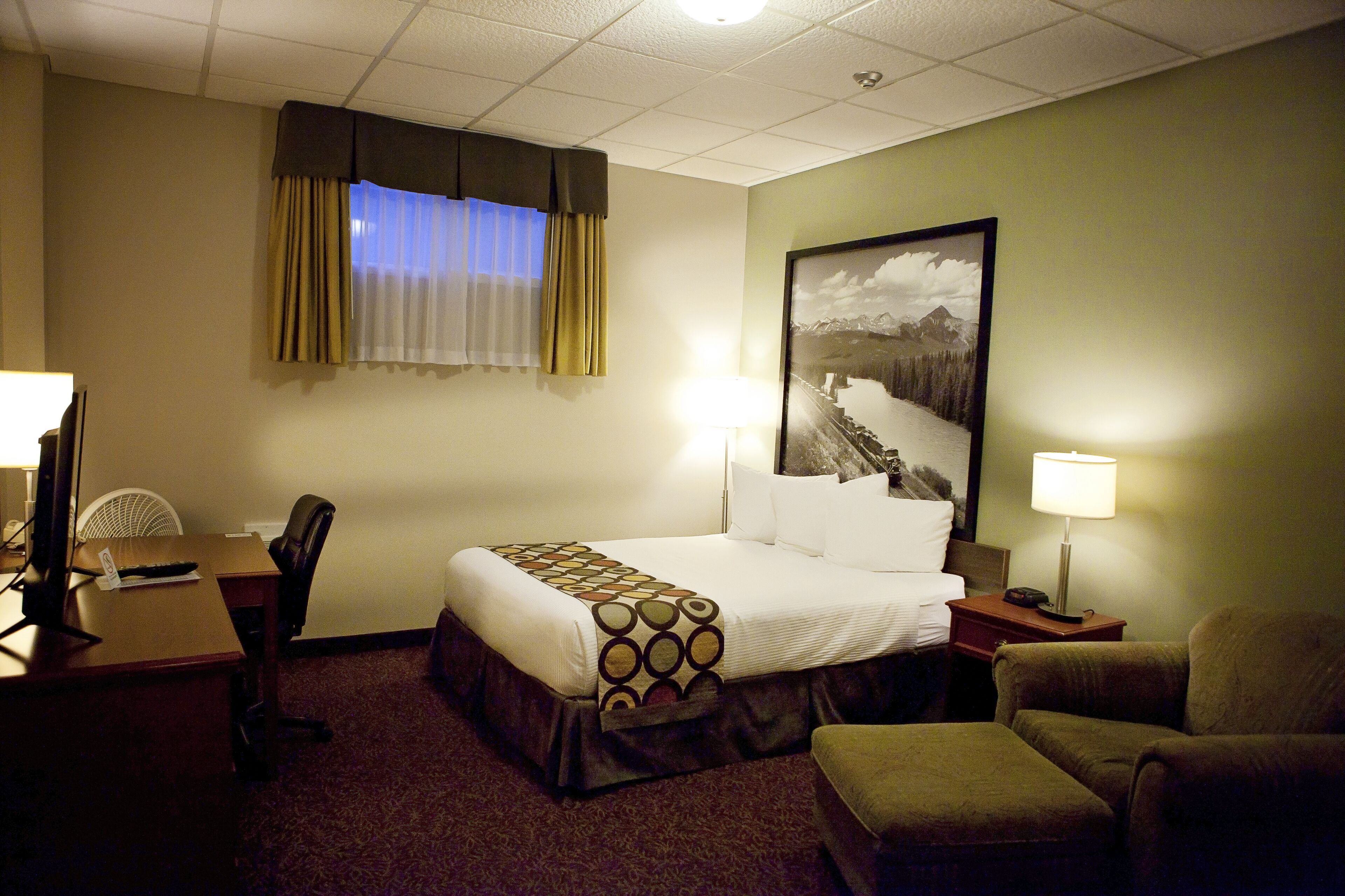 Quarto de hotel com cama, escrivaninha, cadeira e duas luminárias.
