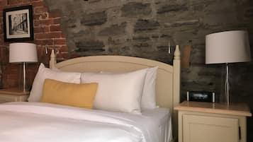 Uma cama com almofadas brancas e amarelas, uma cabeceira de madeira e uma mesa de cabeceira com abajur e relógio digital.