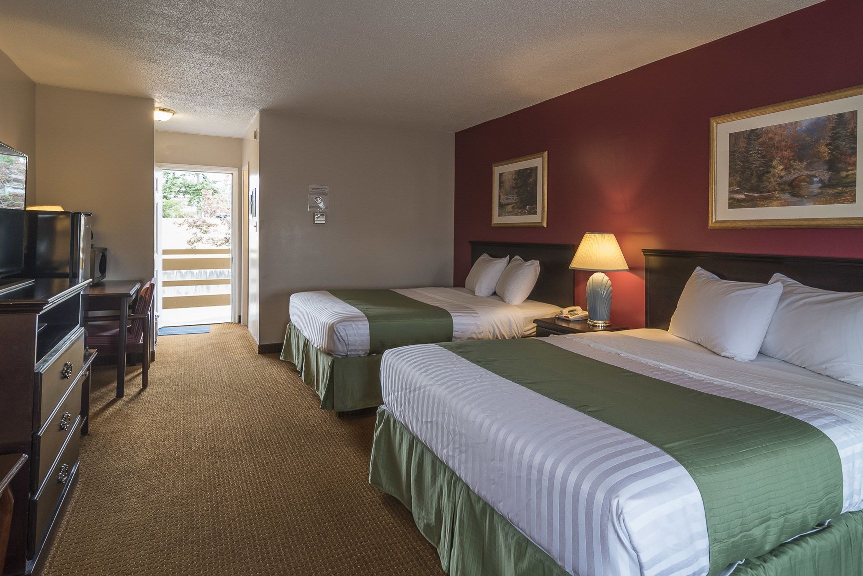 Quarto de hotel com duas camas, uma secretária com cadeira, televisão e um quadro na parede.