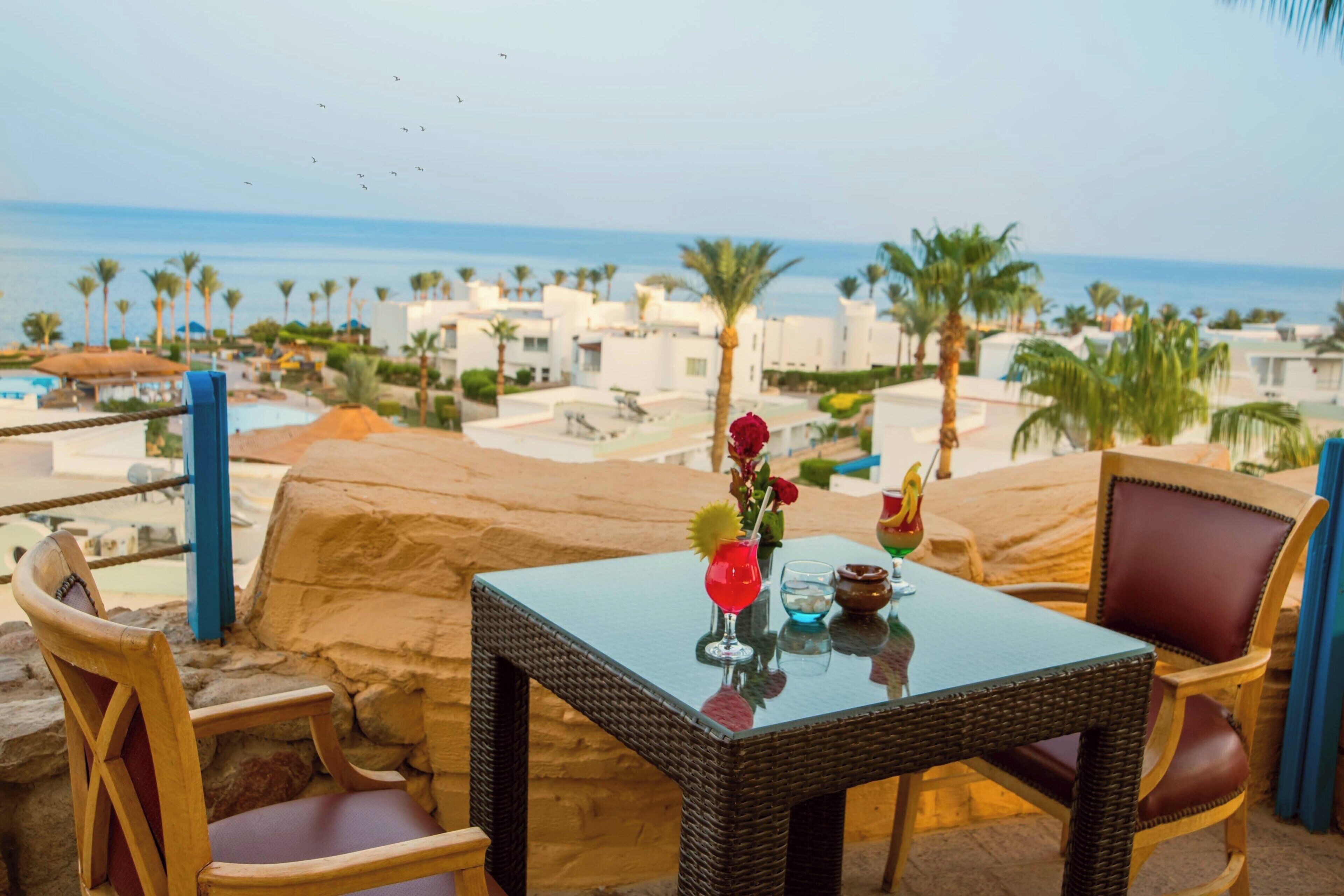 Mesa e cadeiras montadas em um terraço com vista para uma praia e edifícios de um resort.