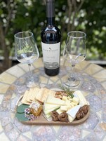 Uma garrafa de vinho rotulada "Black Stallion" e dois copos sobre uma mesa com uma tábua de queijos e biscoitos.