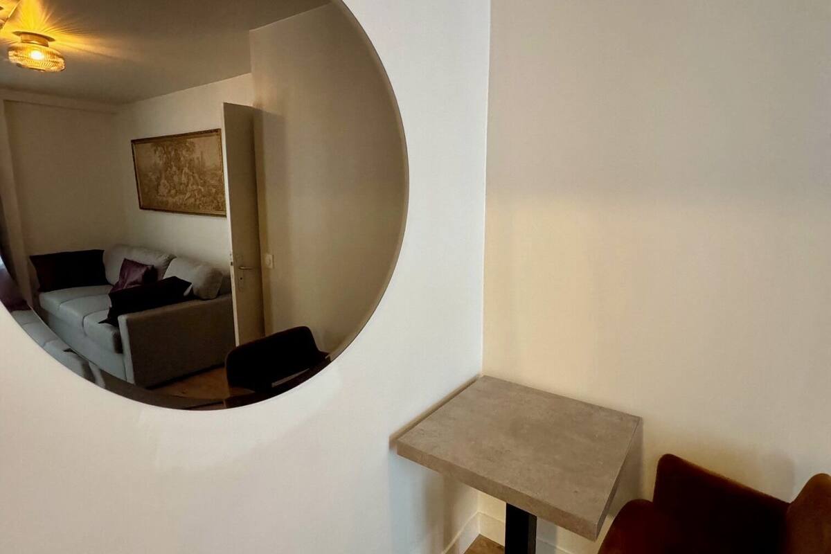 Um quarto com uma janela circular, uma pequena mesa, uma cadeira e um sofá com almofadas.