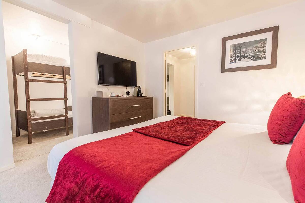 Um quarto com uma cama beliche, uma televisão de tela plana, uma cômoda, um cobertor vermelho e um quadro na parede.