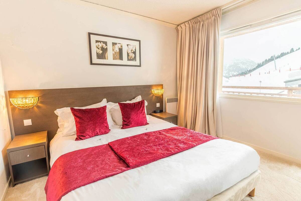 Quarto de hotel com uma cama grande, duas mesas de cabeceira com luminárias, um quadro emoldurado acima da cama e uma janela com cortinas.