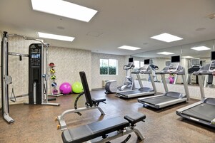 Uma academia com diversos equipamentos de exercício, incluindo esteiras, um banco de musculação e uma máquina de polia.