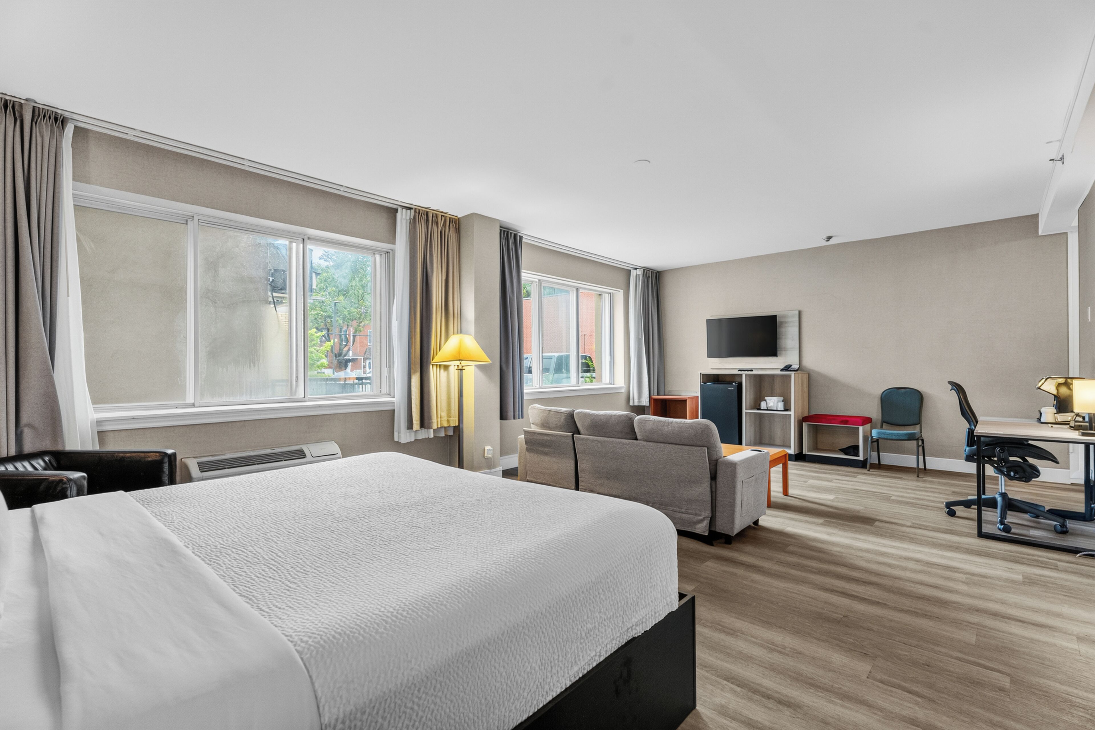 Quarto de hotel com cama, escrivaninha, cadeira, televisão e janela com cortinas.