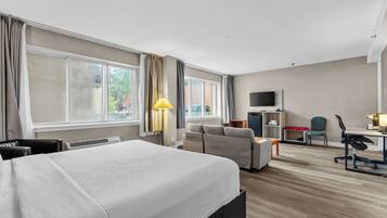 Quarto de hotel com cama, escrivaninha, cadeira, televisão e janela com cortinas.