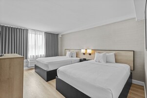 Quarto de hotel com duas camas, uma escrivaninha e uma janela com cortinas.