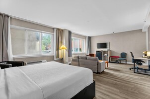 Quarto de hotel com cama, escrivaninha, cadeira, televisão e janelas amplas.