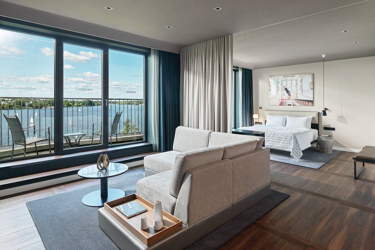 Quarto de hotel moderno com uma varanda grande, um sofá, uma cama e uma mesa de jantar.
