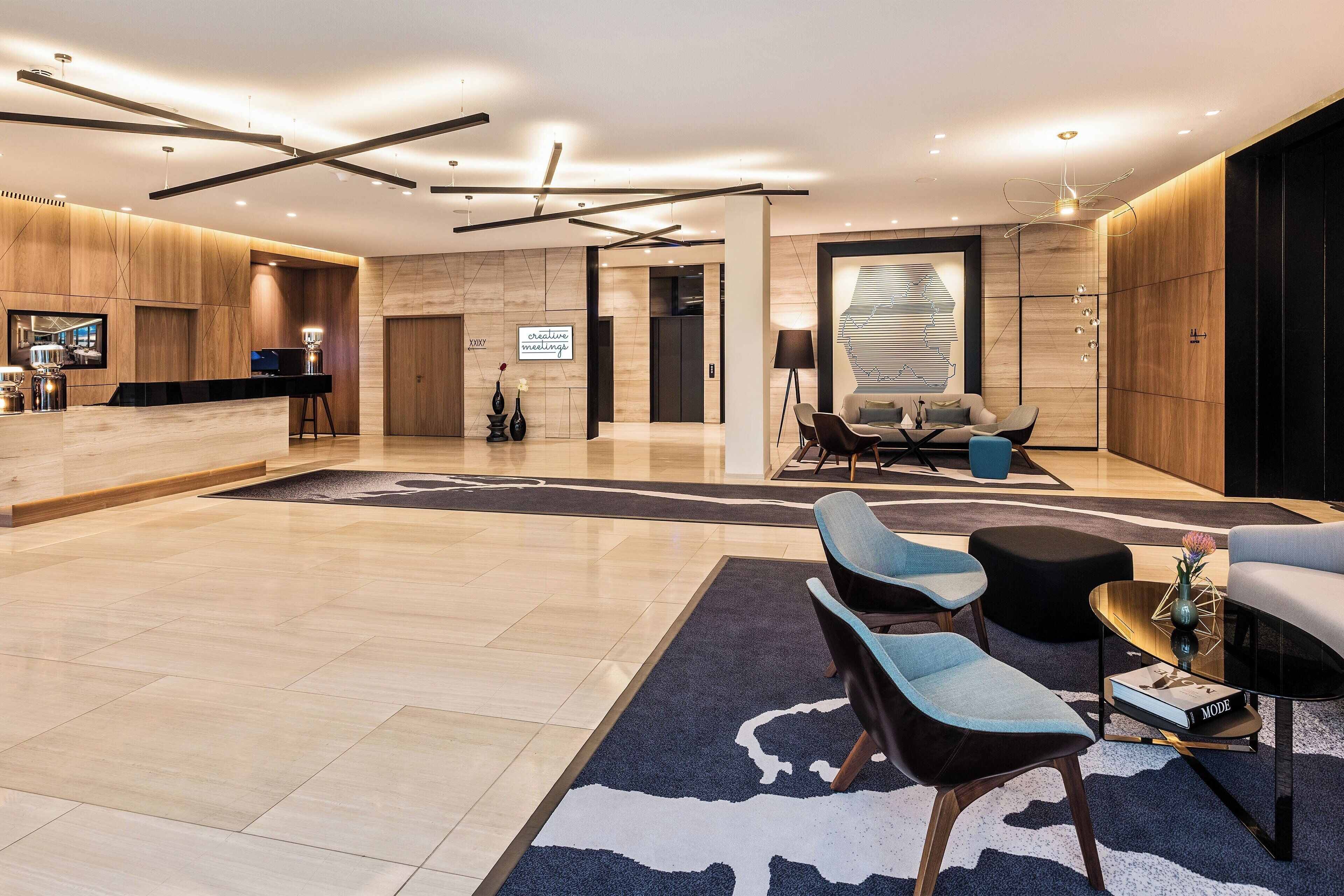 Um lobby de hotel moderno com balcão de recepção, área de estar e uma tela grande.