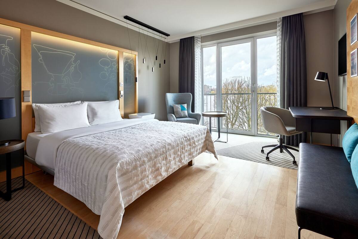 Quarto de hotel moderno com uma cama grande, uma mesa, uma cadeira e uma varanda com vista.