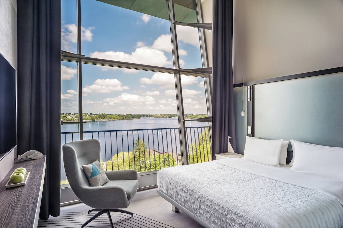 Quarto de hotel com uma janela grande que oferece vista para um lago e vegetação.