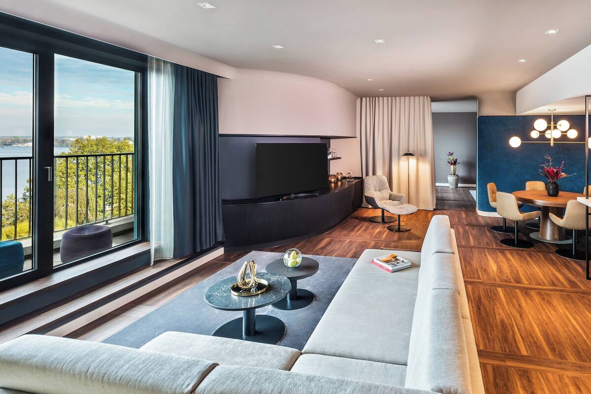 Uma sala de estar moderna com uma televisão grande, um sofá, uma área de refeições e uma varanda com vista para a cidade.