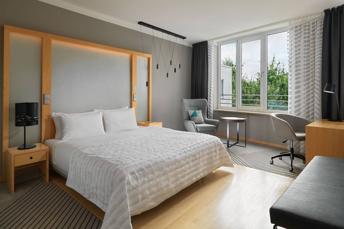 Quarto de hotel com uma cama grande, uma mesa, uma cadeira e uma janela com cortinas.