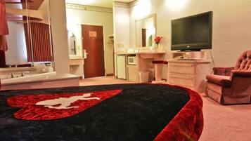 Quarto de hotel com cama, televisão, poltrona, escrivaninha e banheiro.