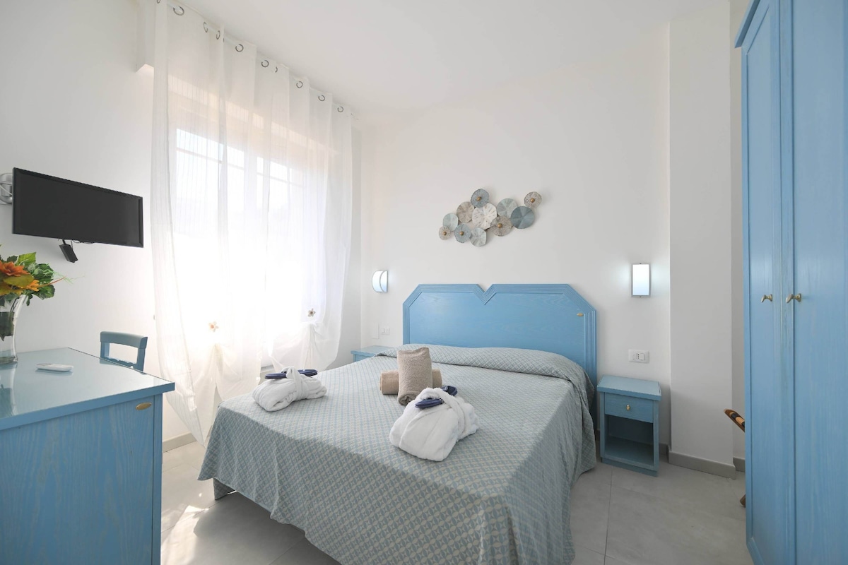 Quarto de hotel com cama, escrivaninha, televisão e guarda-roupa.