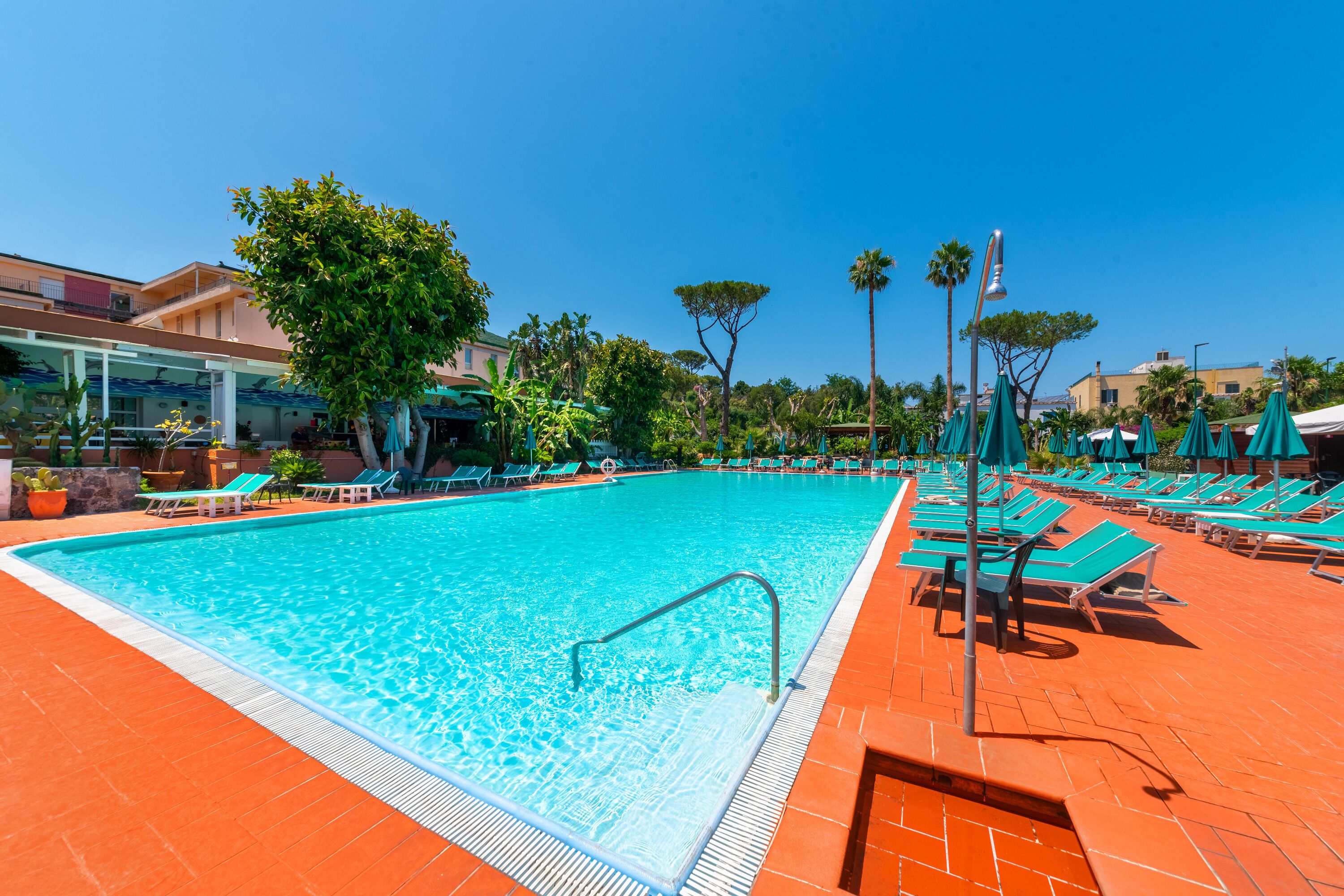 Piscina com águas cristalinas azuis, rodeada por espreguiçadeiras e guarda-sóis, e um deck revestido com azulejos.