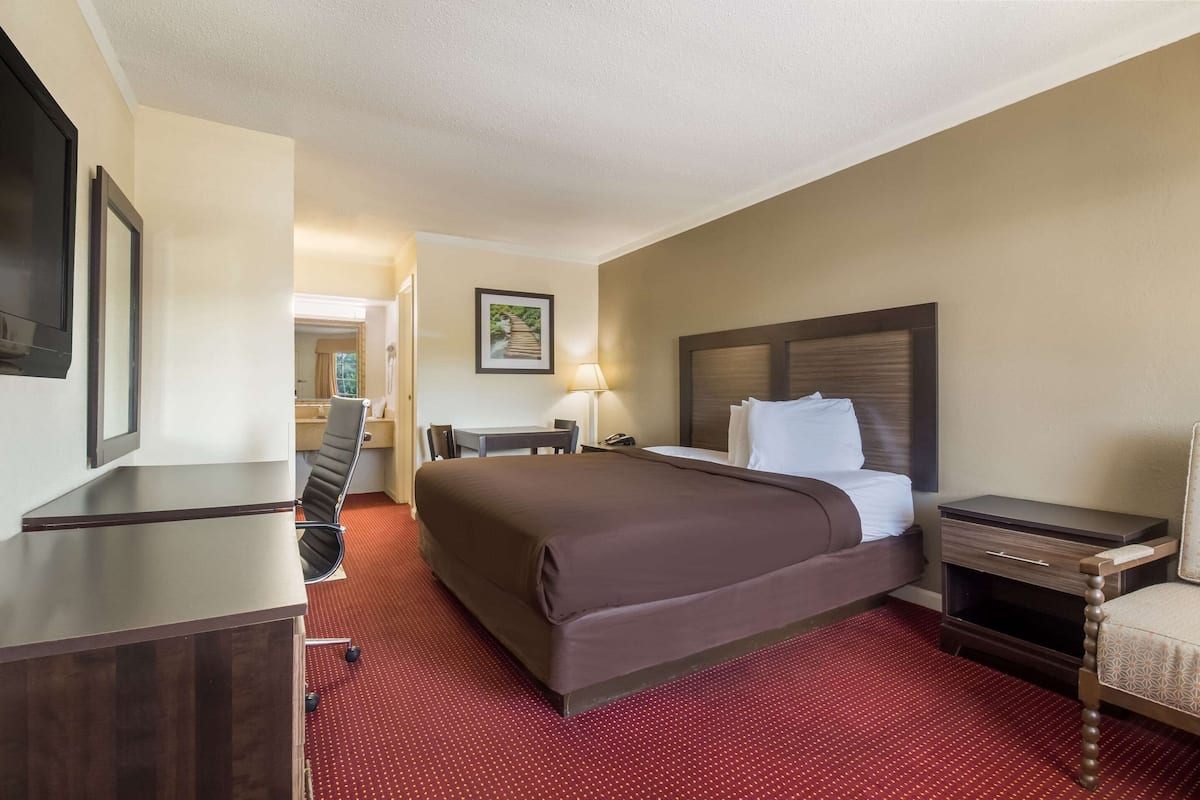 Quarto de hotel com uma cama grande, uma escrivaninha, uma cadeira e uma mesa de cabeceira.