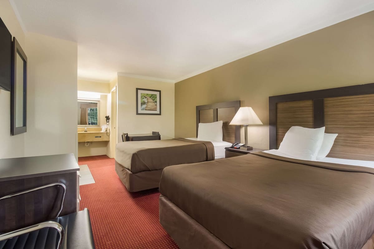 Quarto de hotel com duas camas, uma escrivaninha, uma cadeira, um abajur e um quadro na parede.