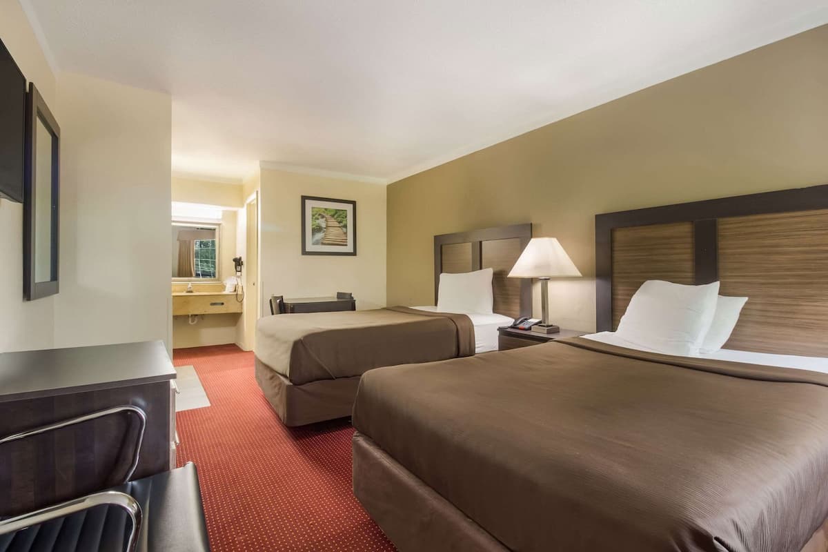 Quarto de hotel com duas camas, uma escrivaninha, uma cadeira, uma mesa de cabeceira e um quadro na parede.