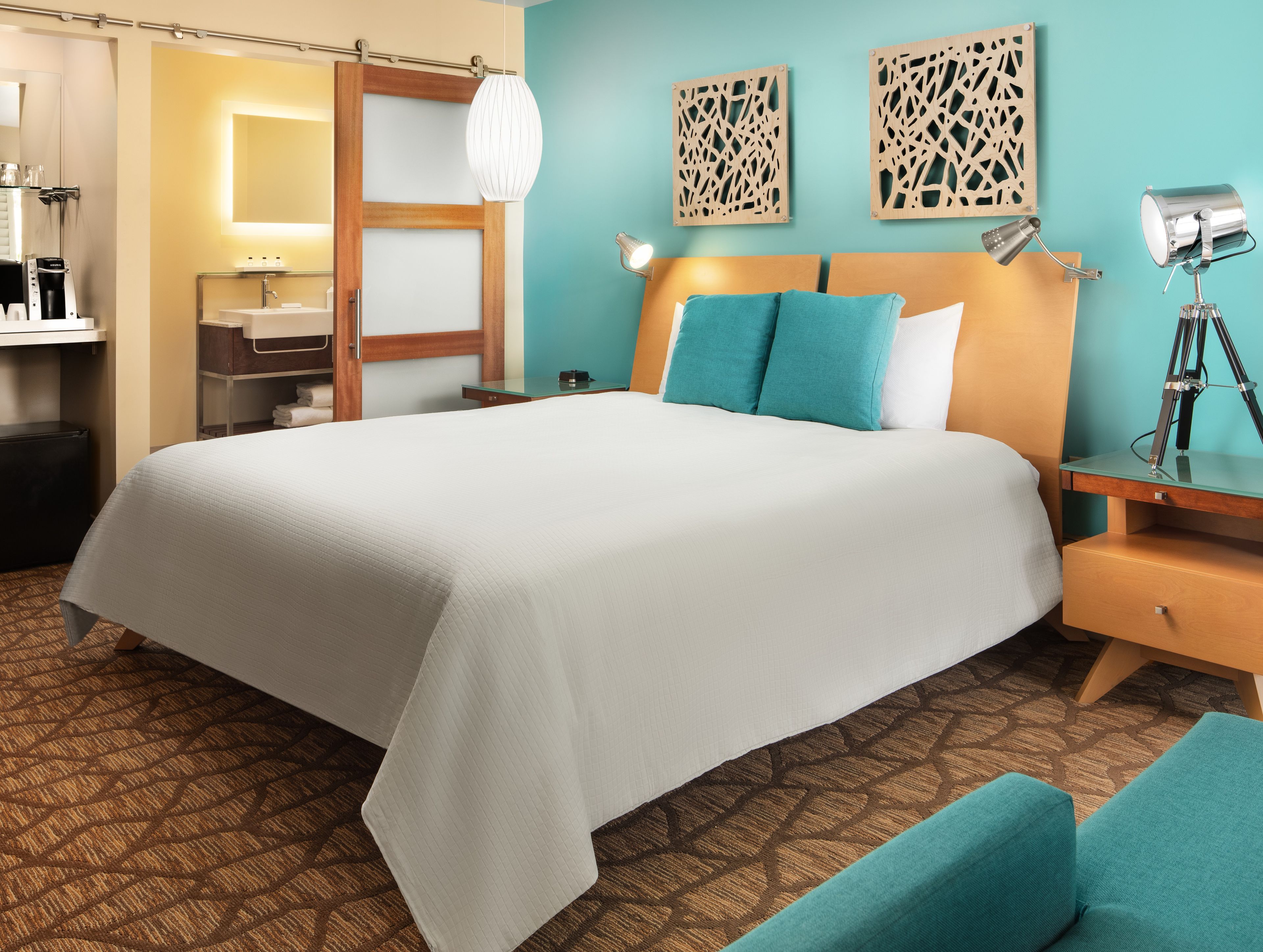 Quarto de hotel com uma cama grande, uma escrivaninha, uma cadeira, um abajur e um espelho.