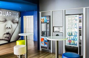 Um interior moderno com parede azul, um pôster grande, máquinas de venda automática e uma pequena mesa com um banquinho amarelo.