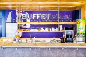 Um balcão de buffet com fundo roxo, diversos alimentos, um dispensador de suco e uma máquina de café.