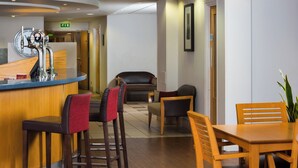 Um saguão de hotel com balcão de recepção, bar, área de estar e um quadro na parede.